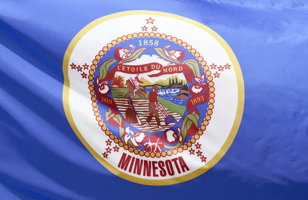 The Minnesota state flag depicts a white settler plowing a field as an ...